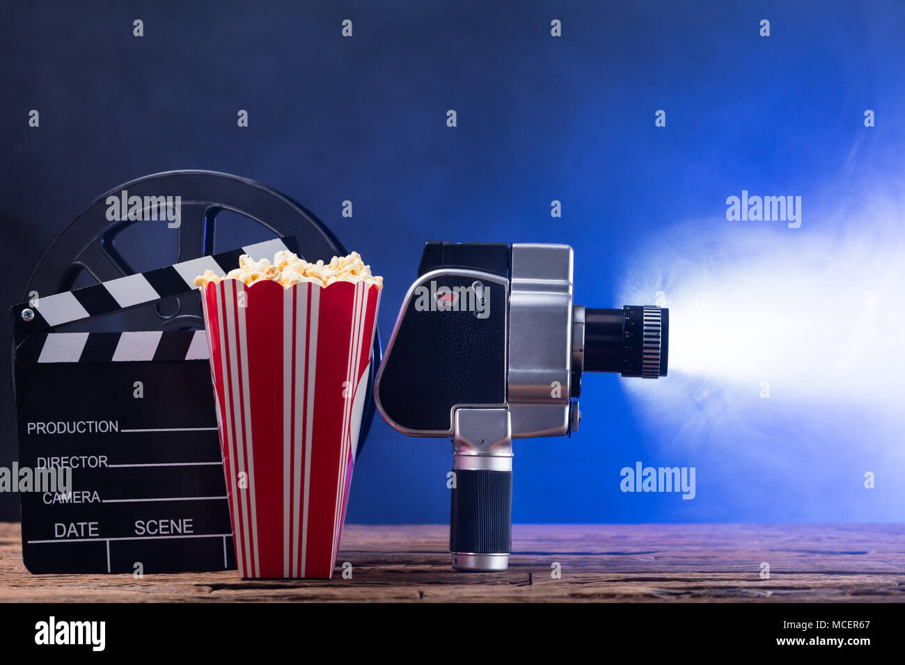 An Illuminated Movie Camera With Popcorn And Clapper Board Against Blue ...