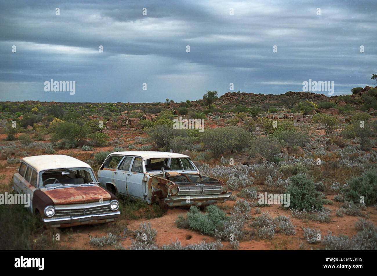 Two wrecked cars abandoned in the outback with a stormy sky behind ...