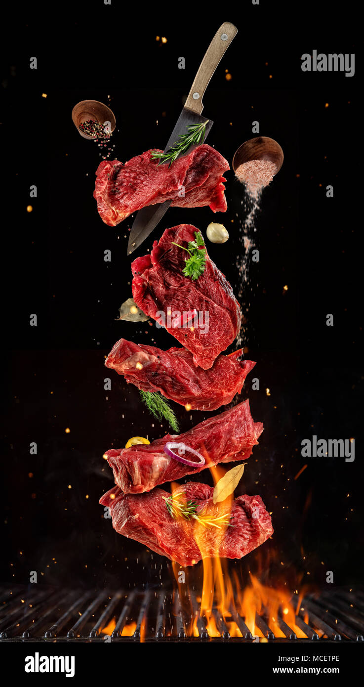 Flying pieces of raw beef steaks from grill grid, isolated on black ...