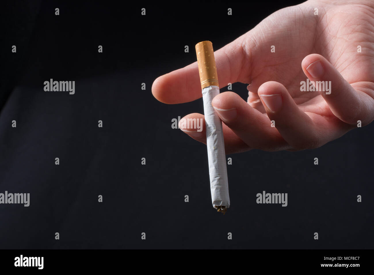 Hand is giving out cigarette on a black background Stock Photo - Alamy
