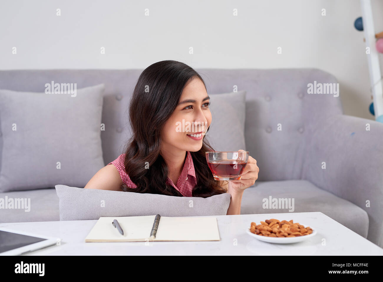 Young asian woman enjoying a tea break and snack while working at home ...