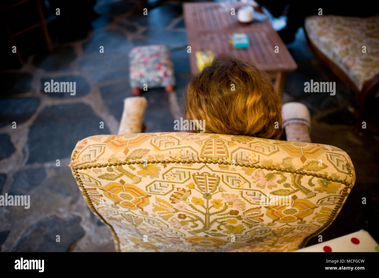 rear view shot looking down onto a woman sitting in an armchair on a ...
