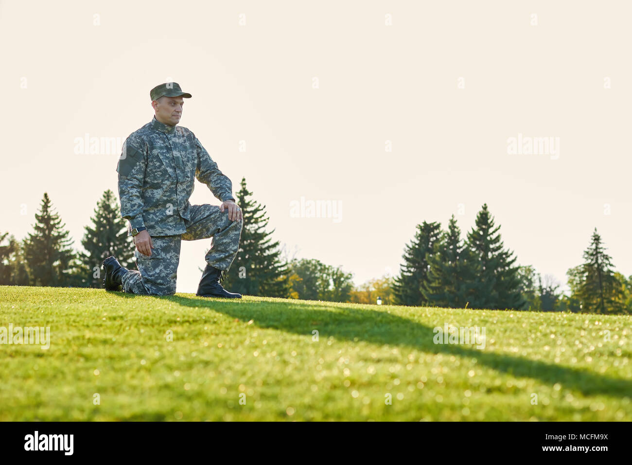 Serious soldier on one knee pose. Soldier stands on one knee outdoor on ...