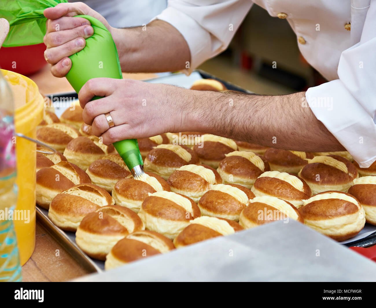 Confectioner is preparing a bun with cream. Squeezes the cream with a ...