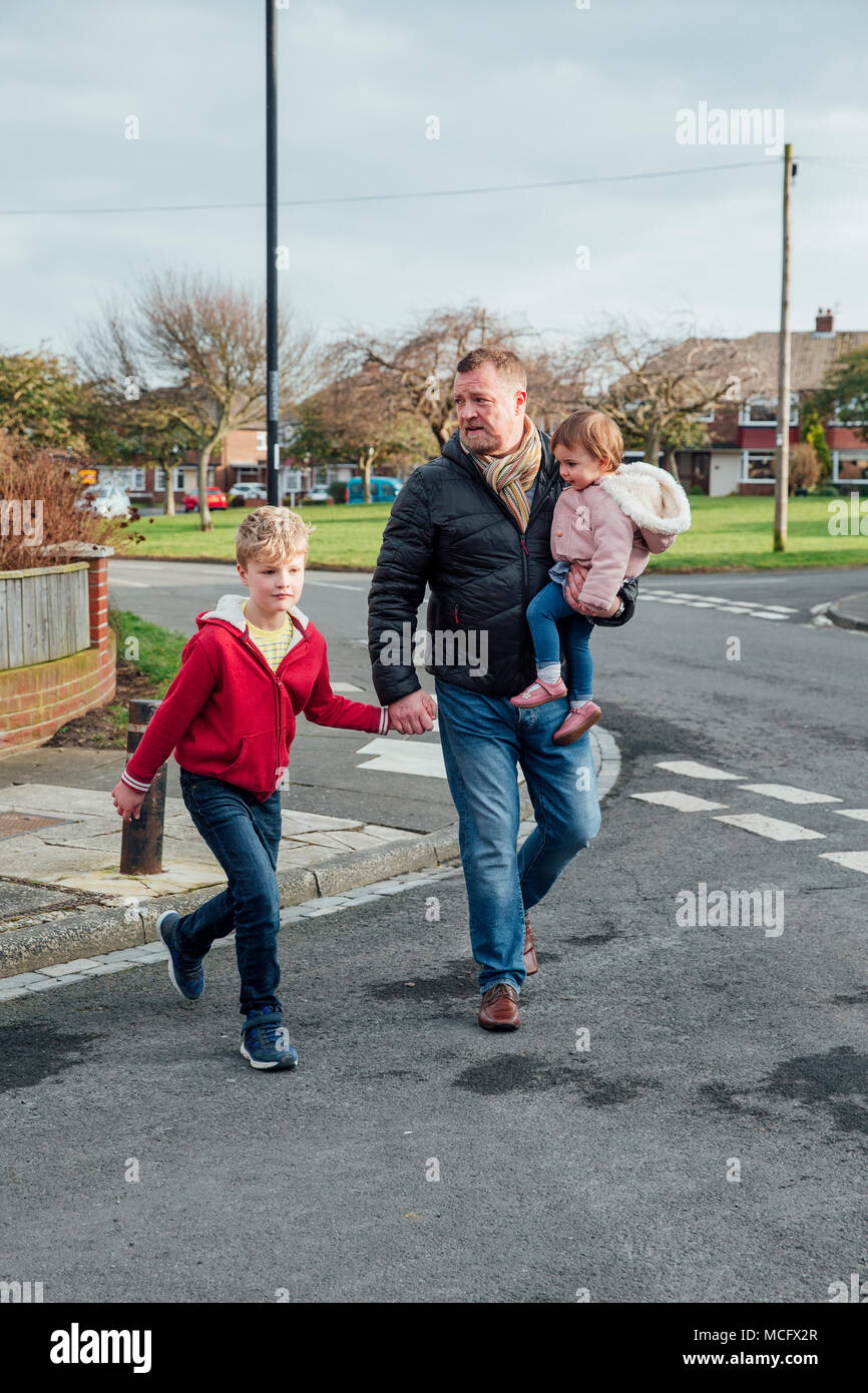 Mature man is crossing the road with his children, his son is holding ...