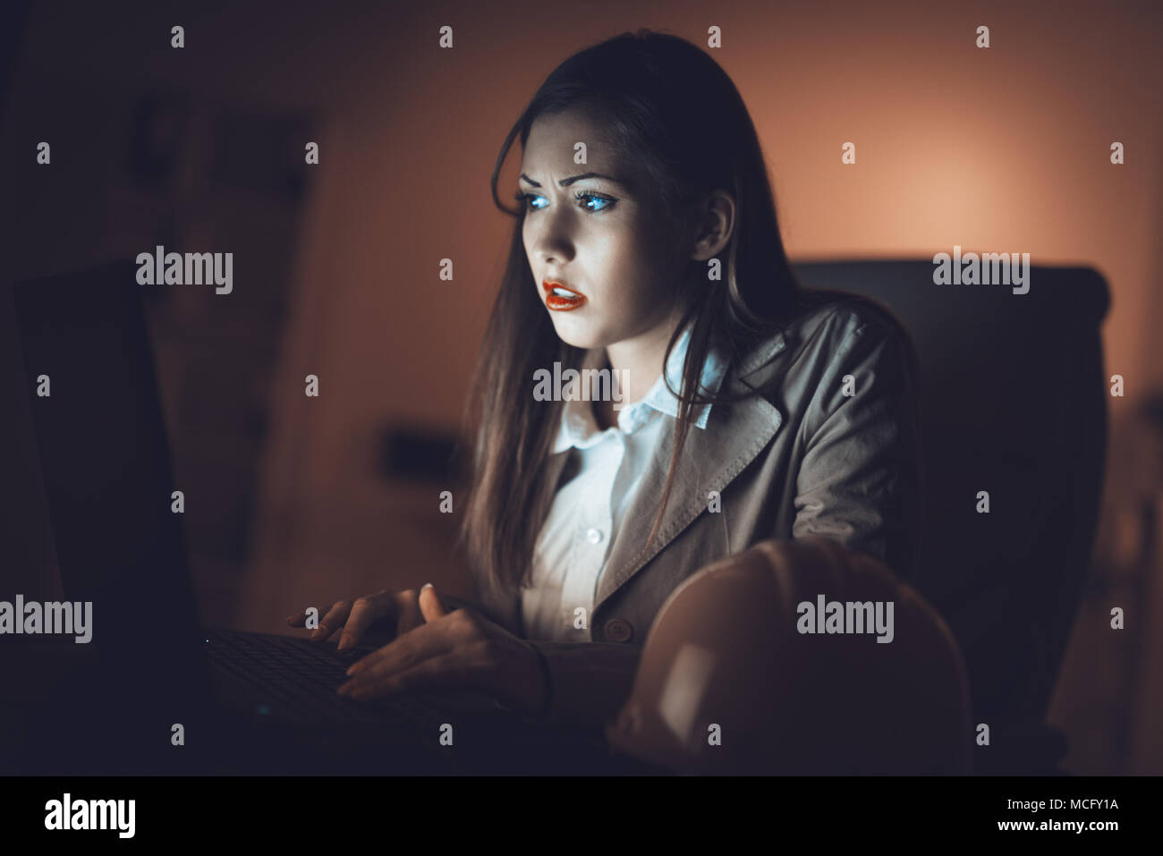 Worried lonely young woman looking at lighted screen of a laptop in ...