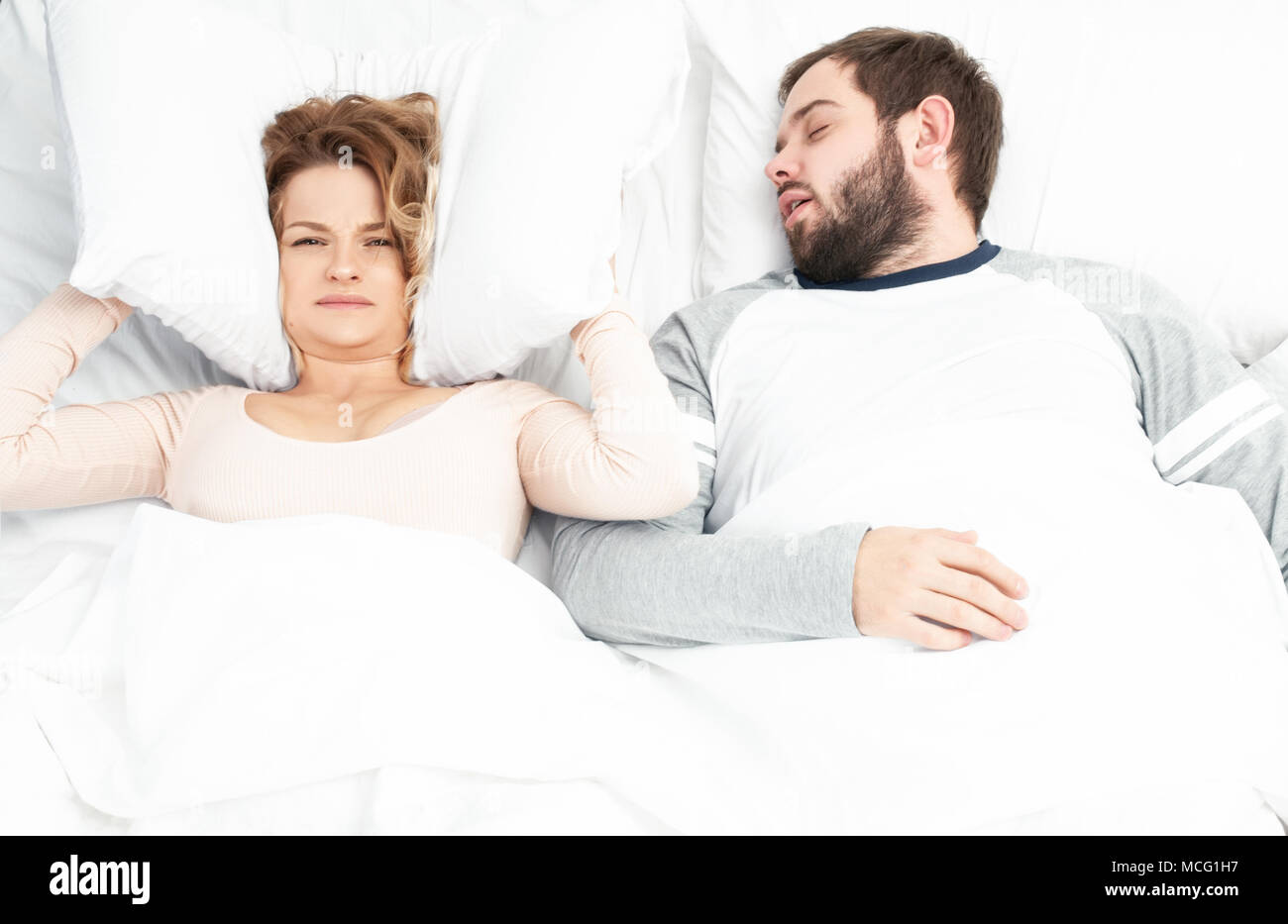 Couple in bed, man snoring and woman can't sleep, covering ears with ...