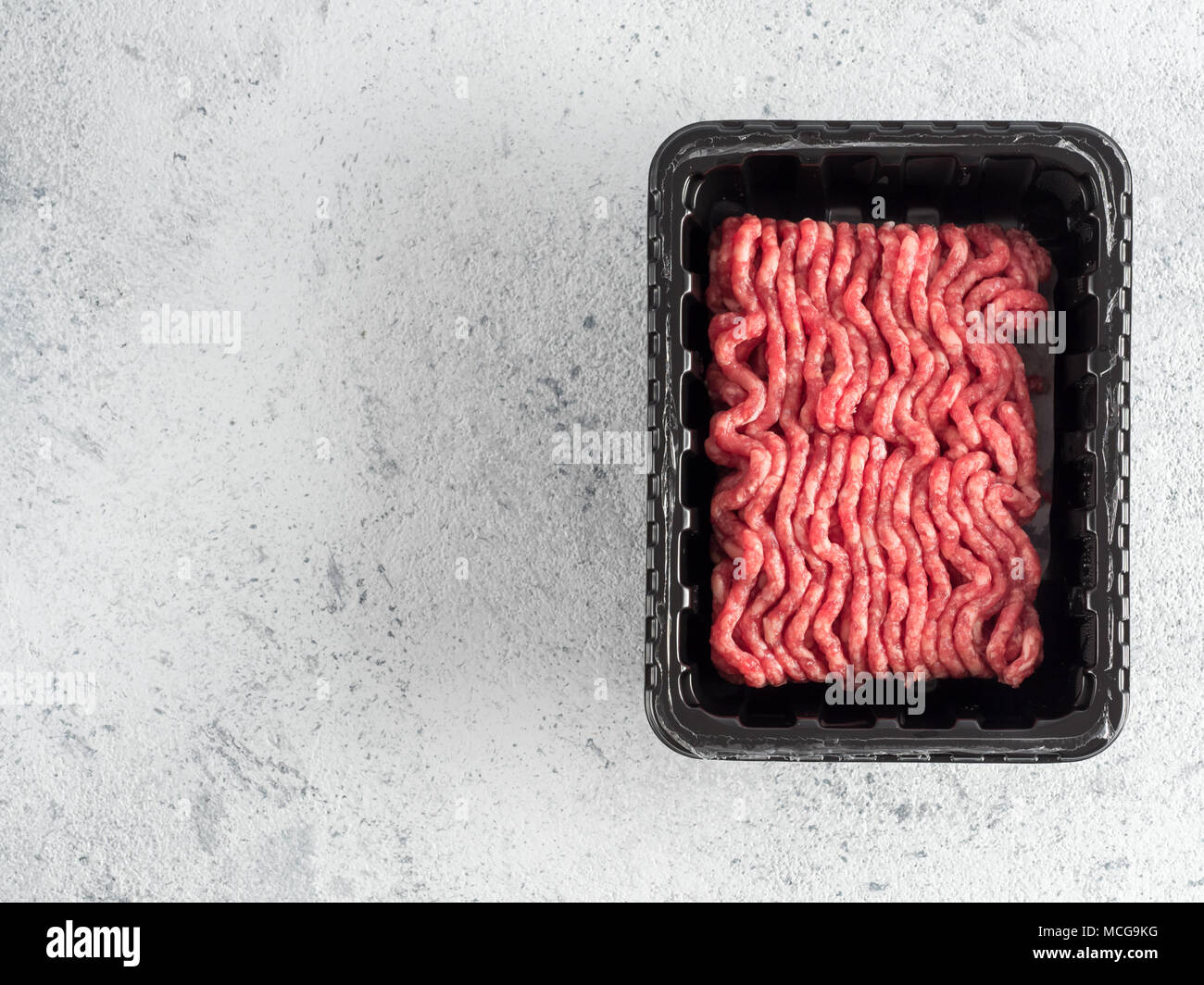 Fresh raw minced beef in plastic tray over light gray cement background ...