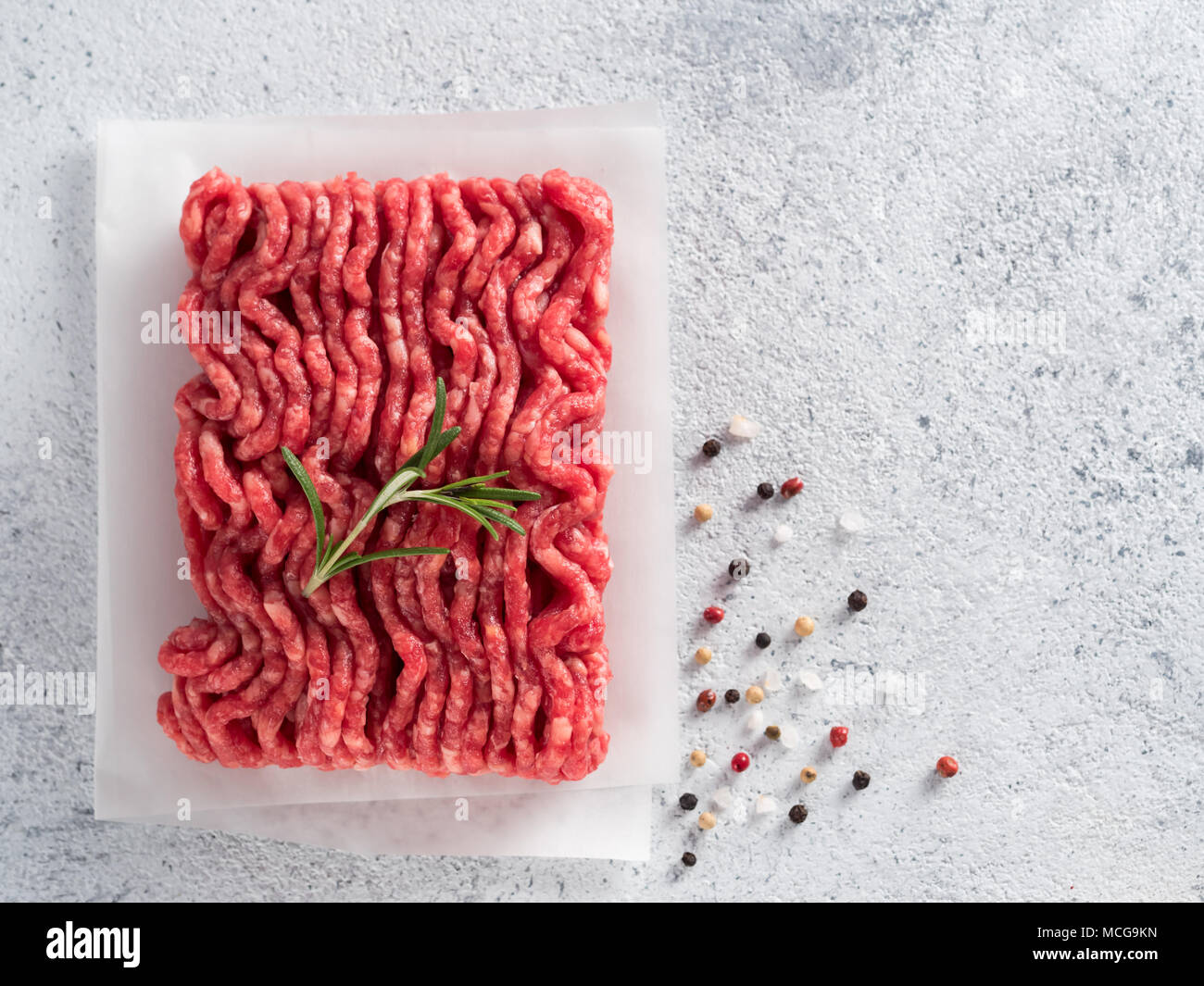 Fresh raw minced beef on backing paper over light gray cement ...