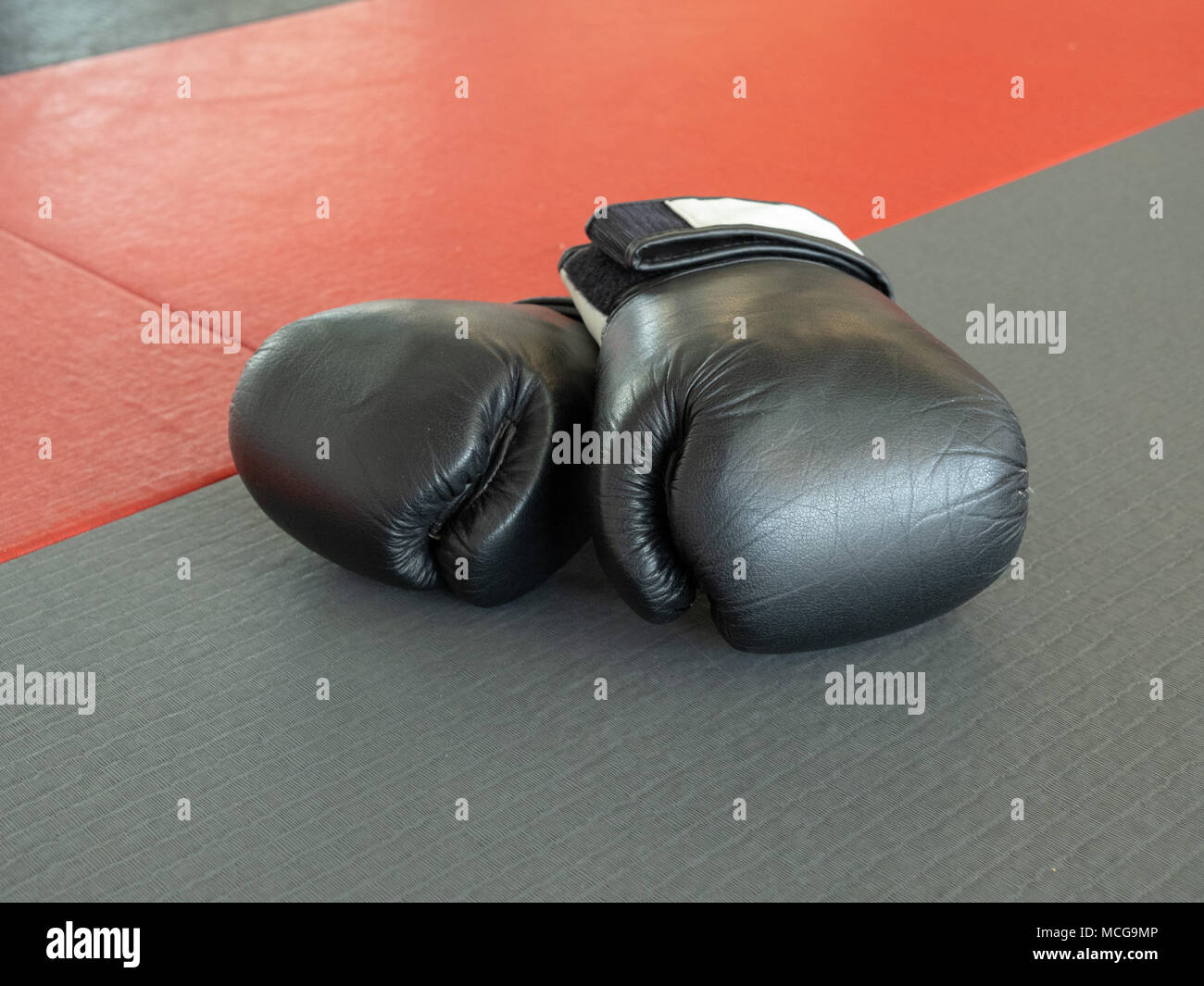 Black boxing gloves sitting on the mats of a boxing gym Stock Photo - Alamy