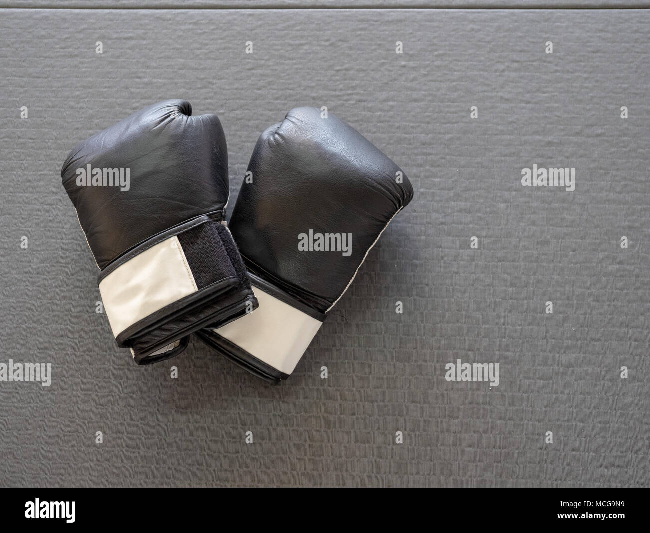 Black boxing gloves sitting on the mats of a boxing gym on grey mats ...