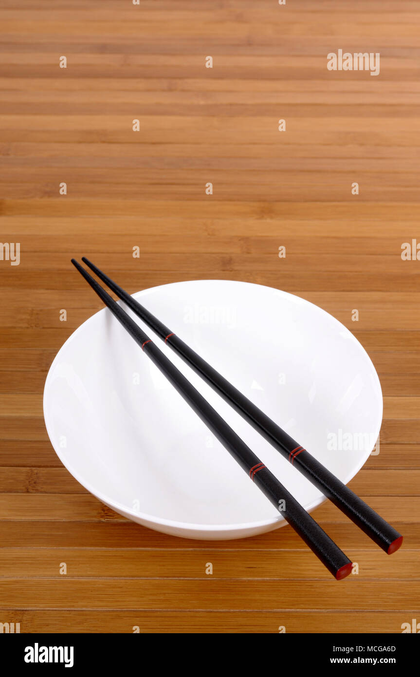 White empty rice bowl with wooden chopsticks on a bamboo background ...