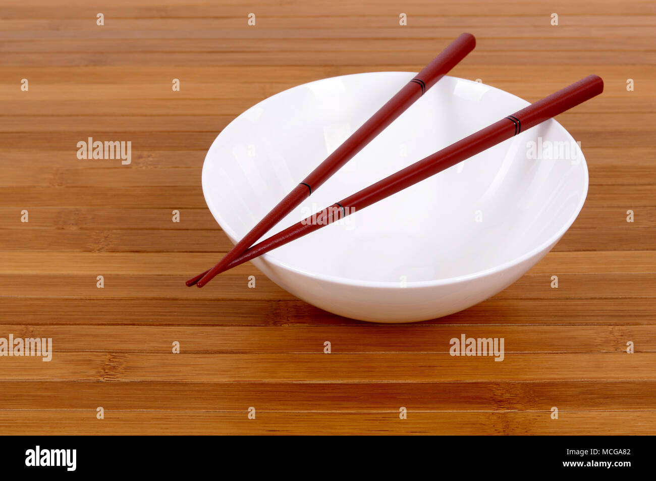 White empty rice bowl with wooden chopsticks on a bamboo background ...
