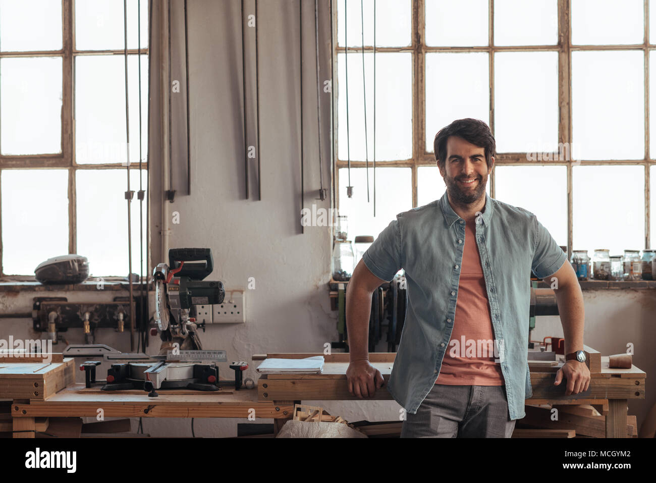 Portrait of a young woodworker smiling confidently while leaning ...