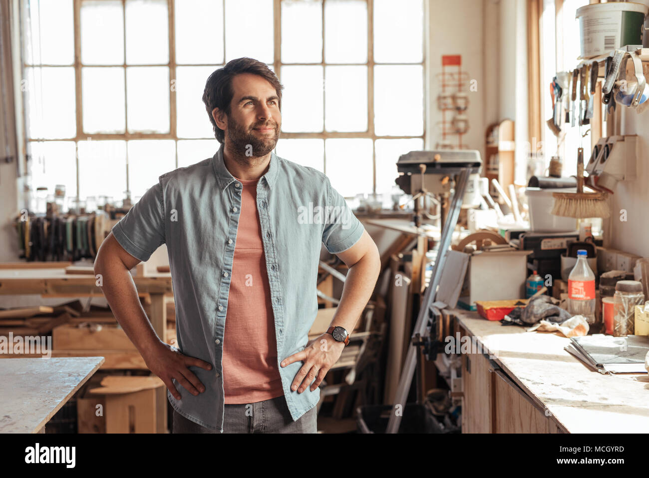Smiling young woodworker thinking up new designs while standing with ...