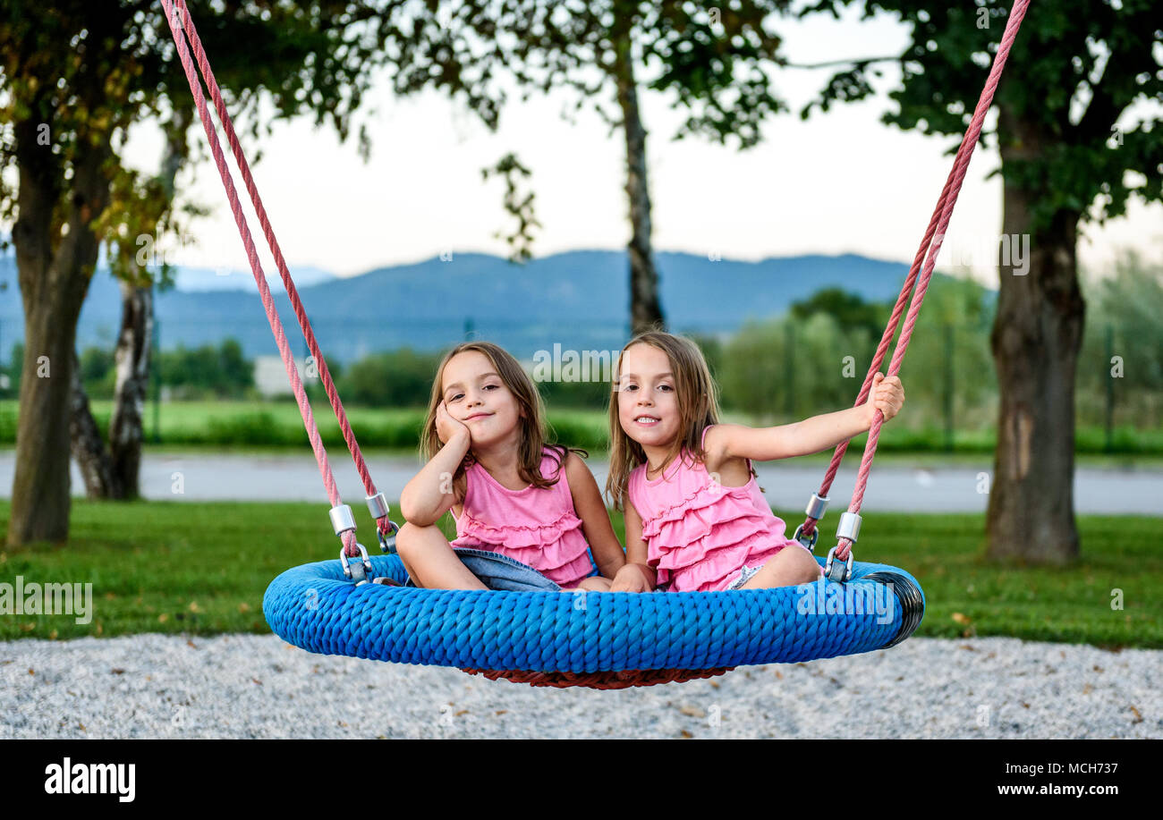 Identical twin girls on spider web nest swing on playground. Active ...