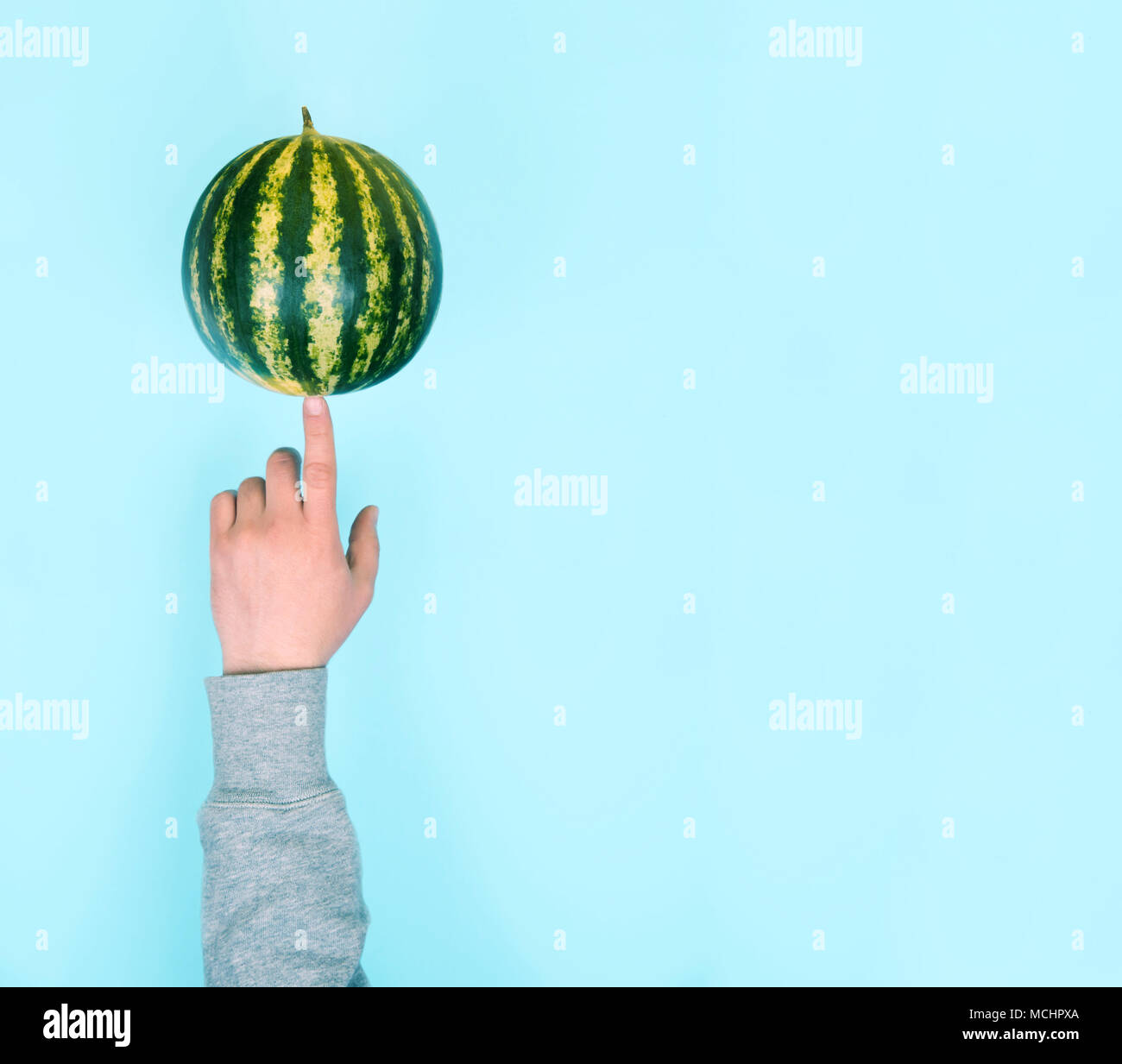 Male hand balancing a watermelon on a finger against blue background ...