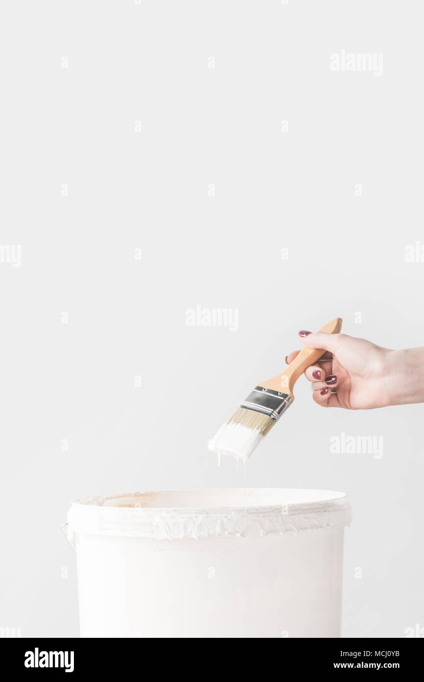 cropped image of woman holding brush in white paint above bucket ...