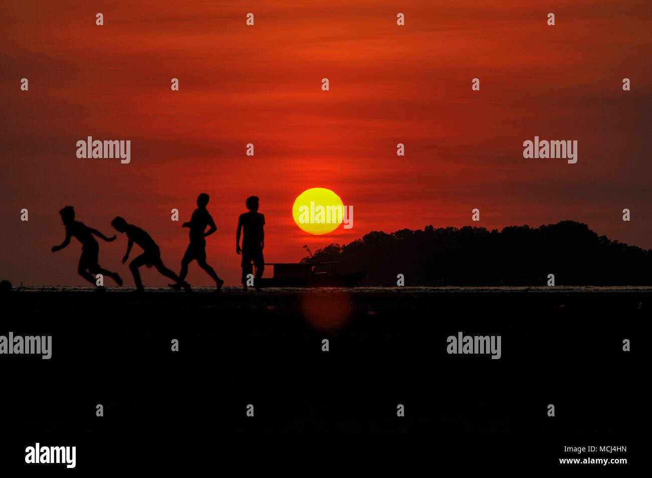 Silhouette of young adults running by the sunset on the beach with ...