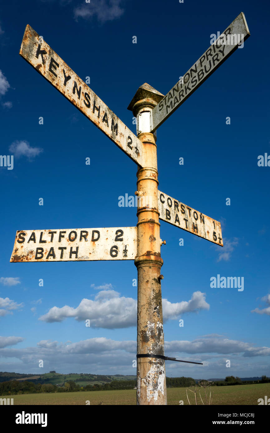 An old rusty signpost with four pointers against a blue sky with white ...