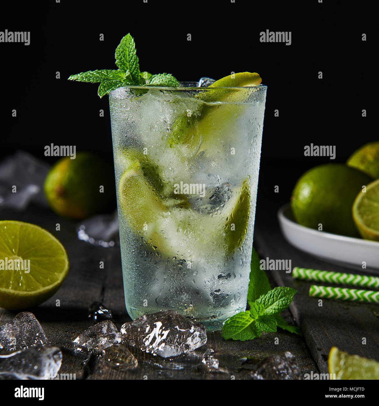 Mojito cocktail with lime and mint in highball glass with ice on a dark wood background. Square ...