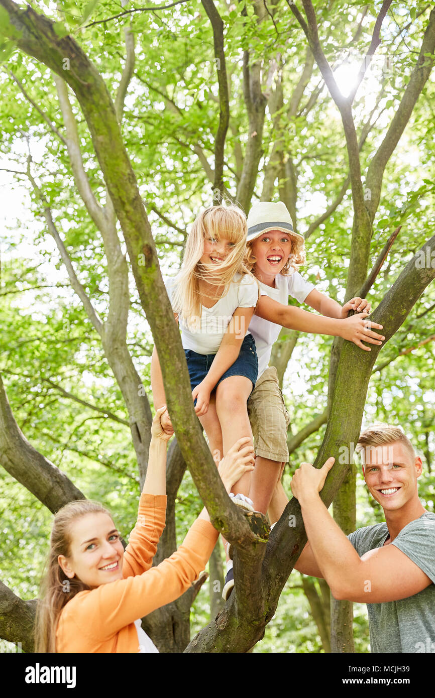 Two children climb on a tree with the help of their parents Stock Photo ...