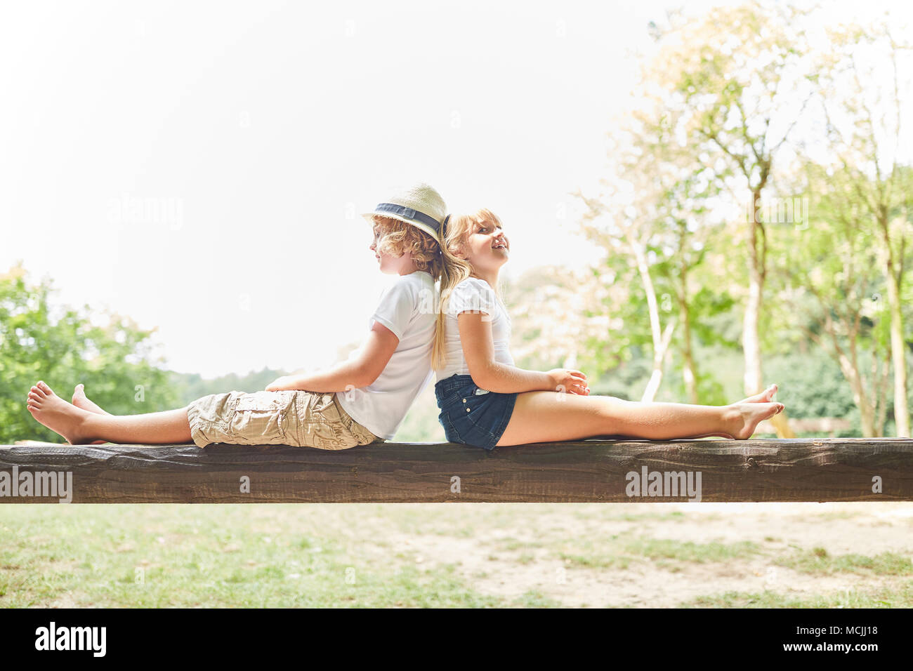 Boy and girl sit relaxed back to back in the park in summer Stock Photo ...