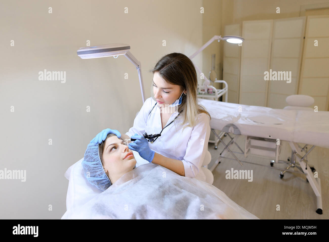Charming woman lying at cosmetology cabinet and getting tattooing ...