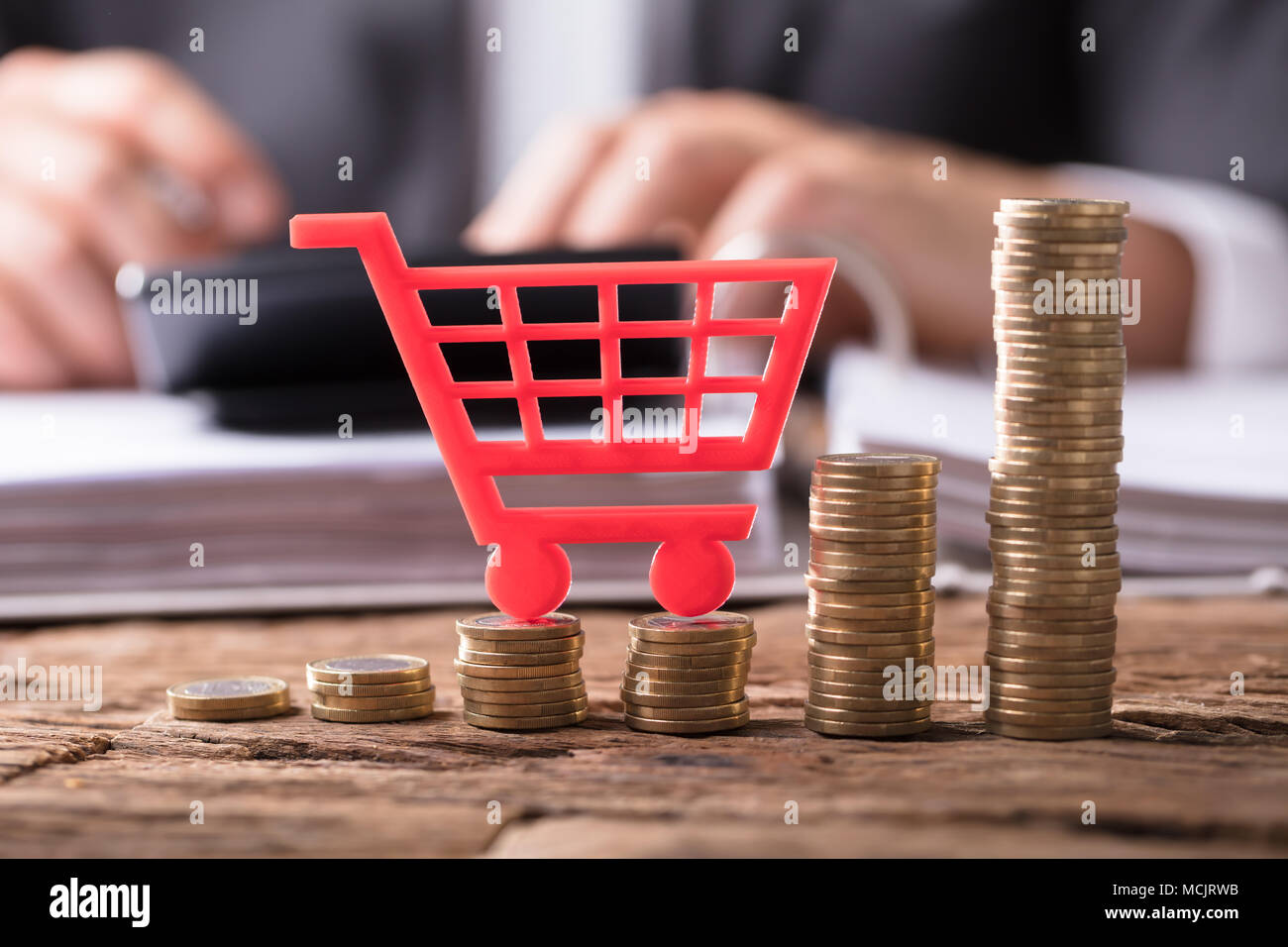 Close-up Of Red Shopping Cart On Stacked Golden Coins Over Wooden Desk ...