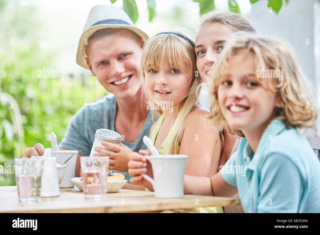 Family and children sit relaxed at the coffee table in summer in the ...
