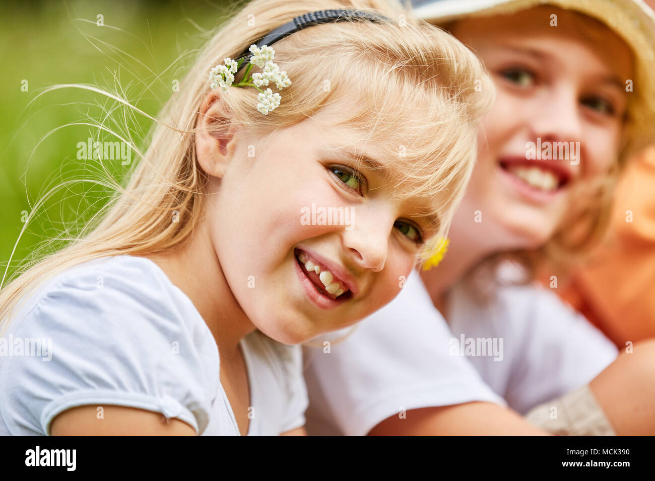 Blond girl with flowers in her hair smiles mischievously and curiously ...