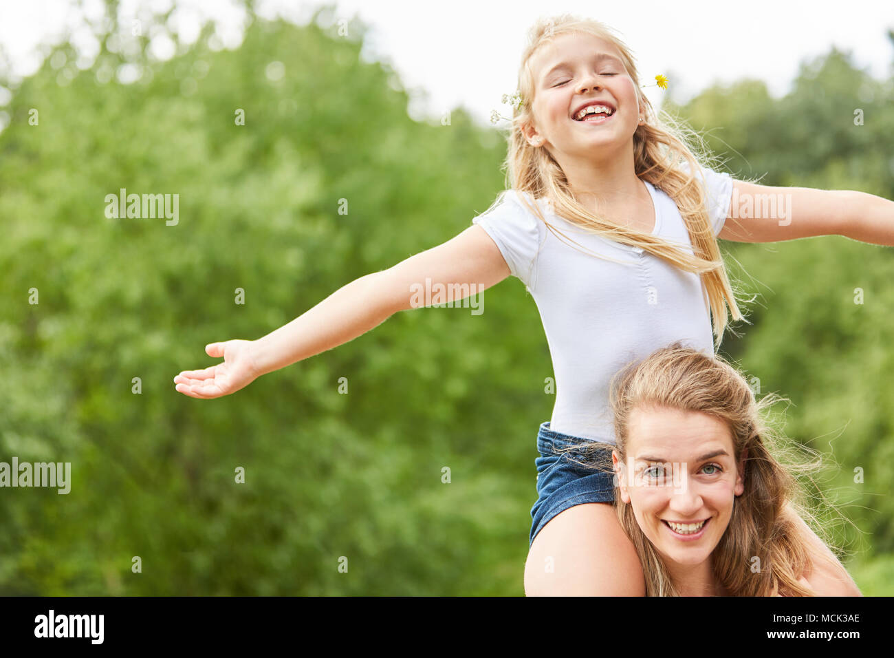 Happy girl is sitting piggyback on mother's back Stock Photo - Alamy