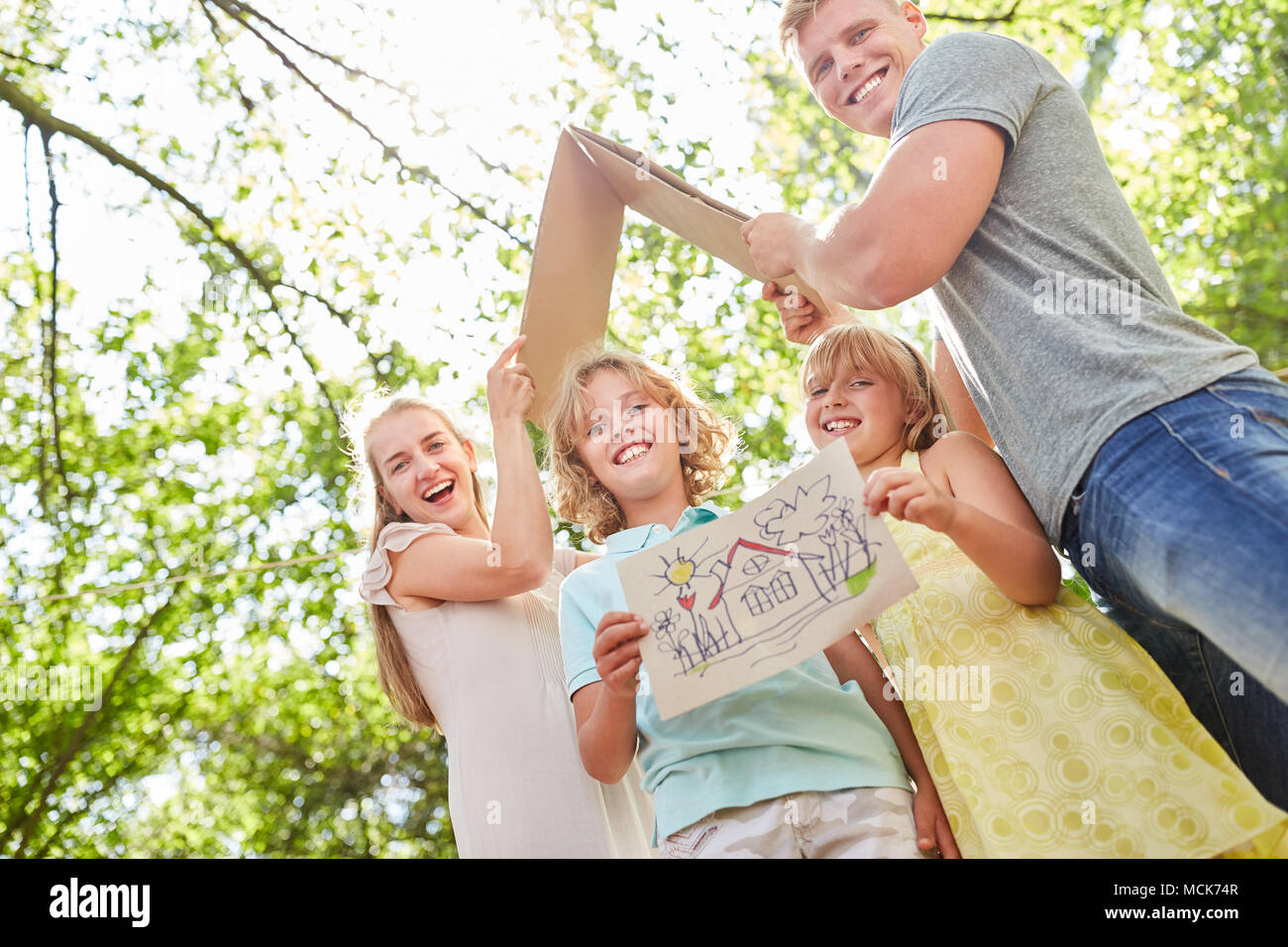 Happy family and children are holding drawing of dream home as a vision ...