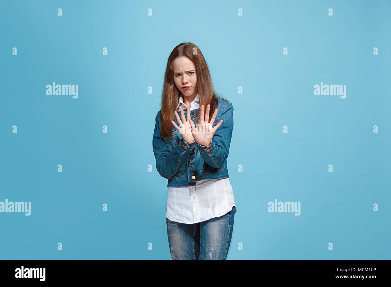 Doubtful pensive teen girl rejecting something against blue background ...