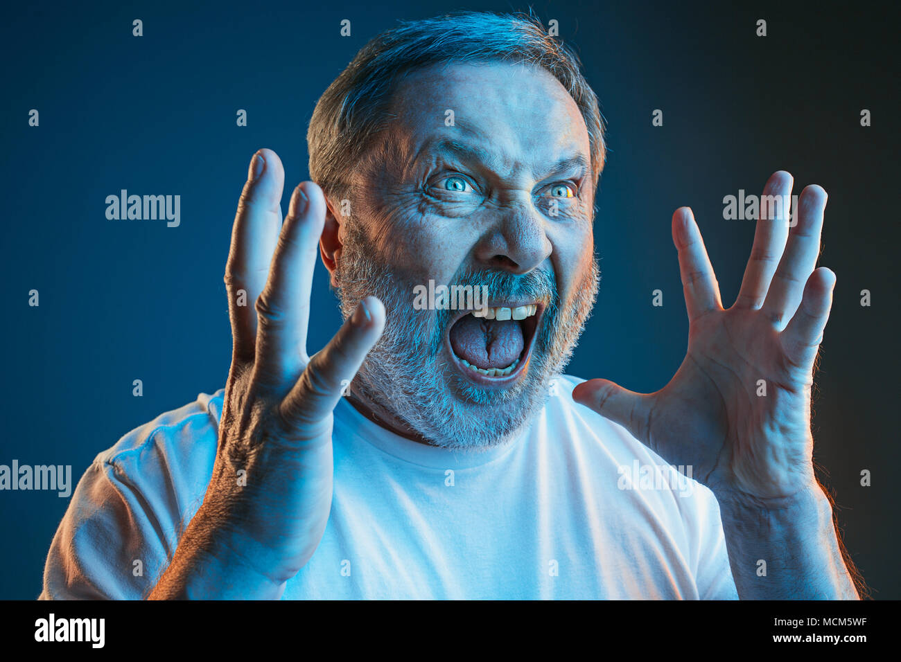 The senior emotional angry man screaming on blue studio background ...