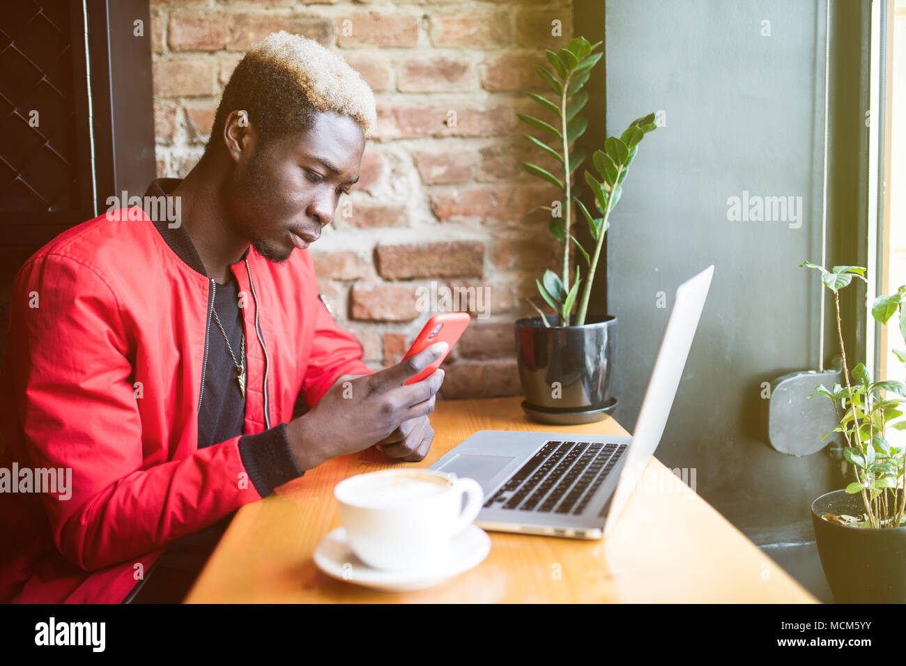 Handsome Afro American guy sitting in cafeteria with phone in hands in ...