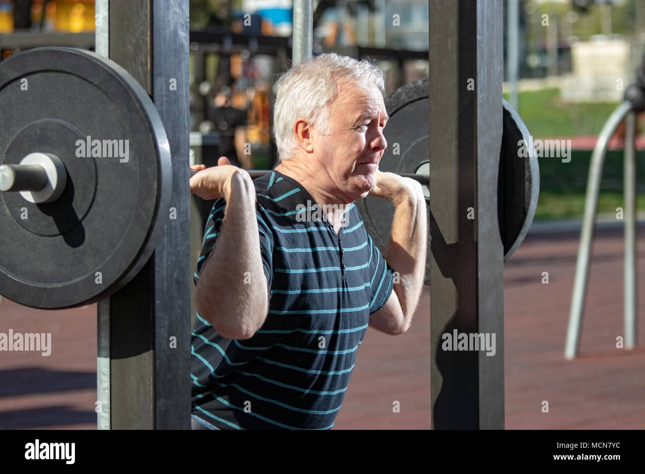 Elderly man making squats with weights in a fitness park (outdoors gym ...