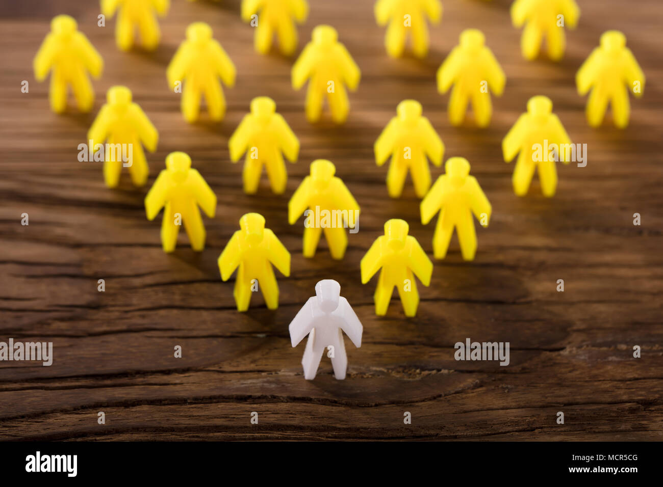 Elevated View Of White Figure Leading Yellow Human Figures On Wooden ...