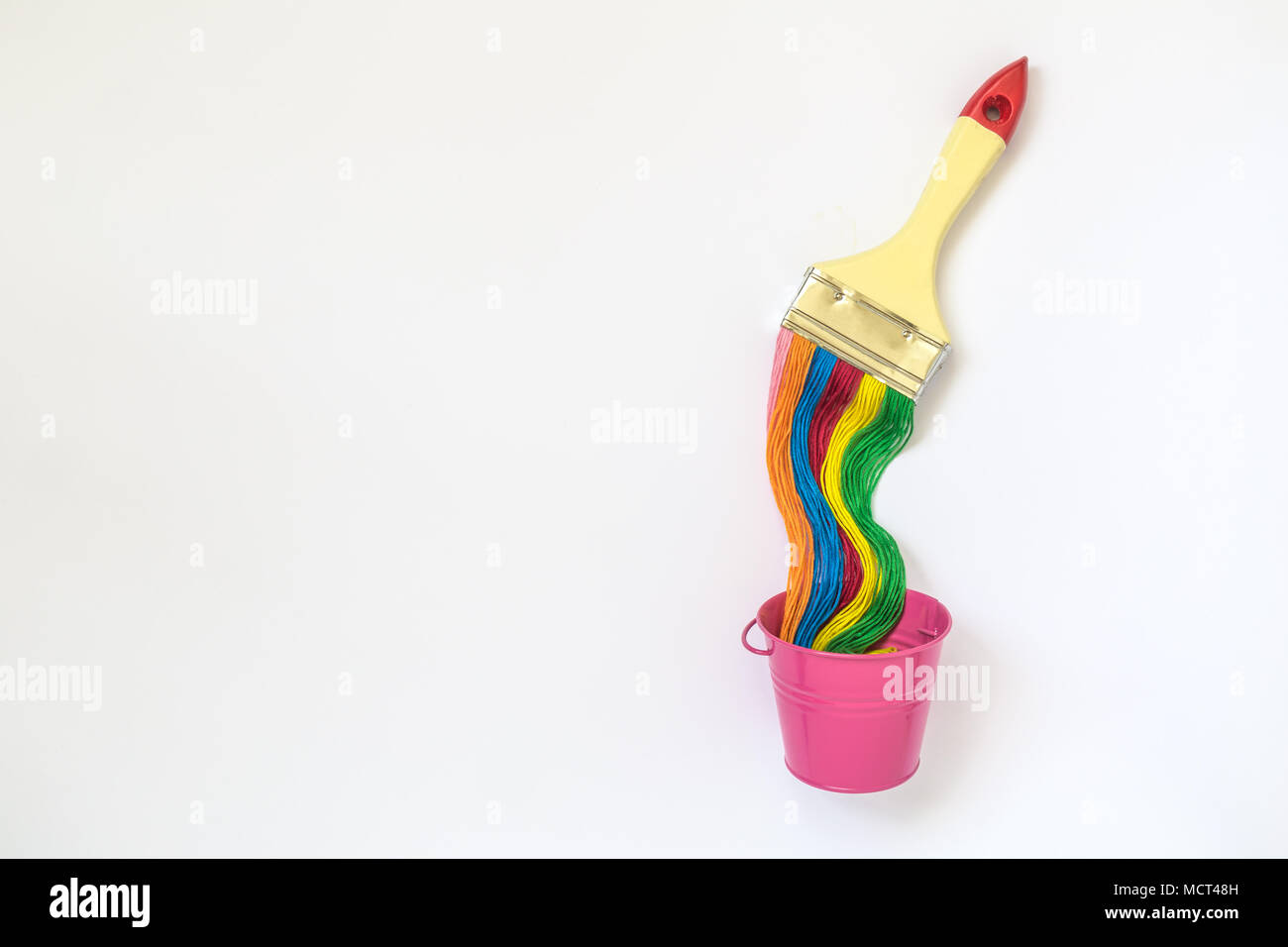 Paint brush with colorful strings and small pink bucket on white ...
