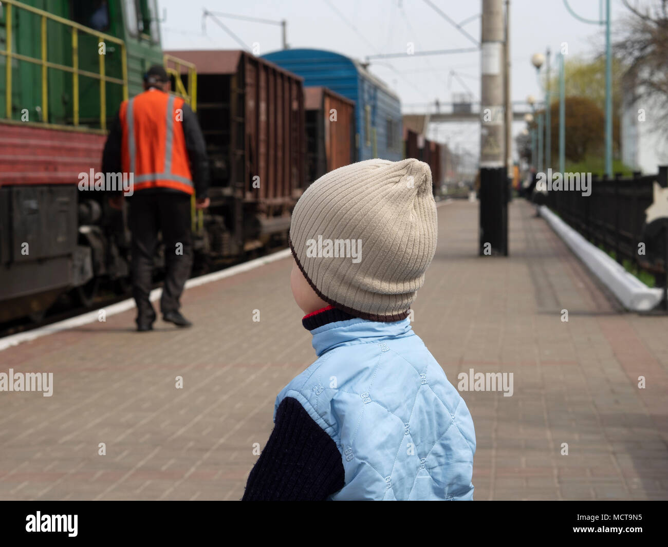 Small Caucasian boy looks at a railwayman walking along a train ...