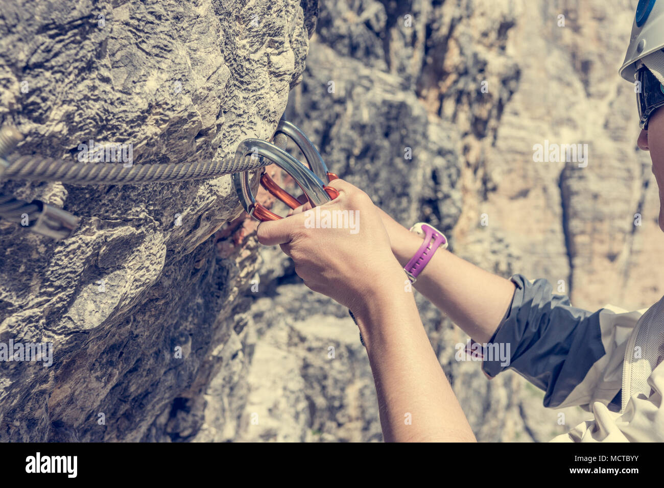 Closeup of female climber attaching via ferrata set to steel cable ...