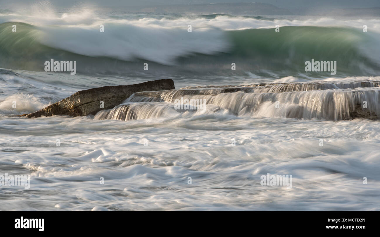 Rocky seashore with wavy ocean and wind waves crashing on the rocks at ...