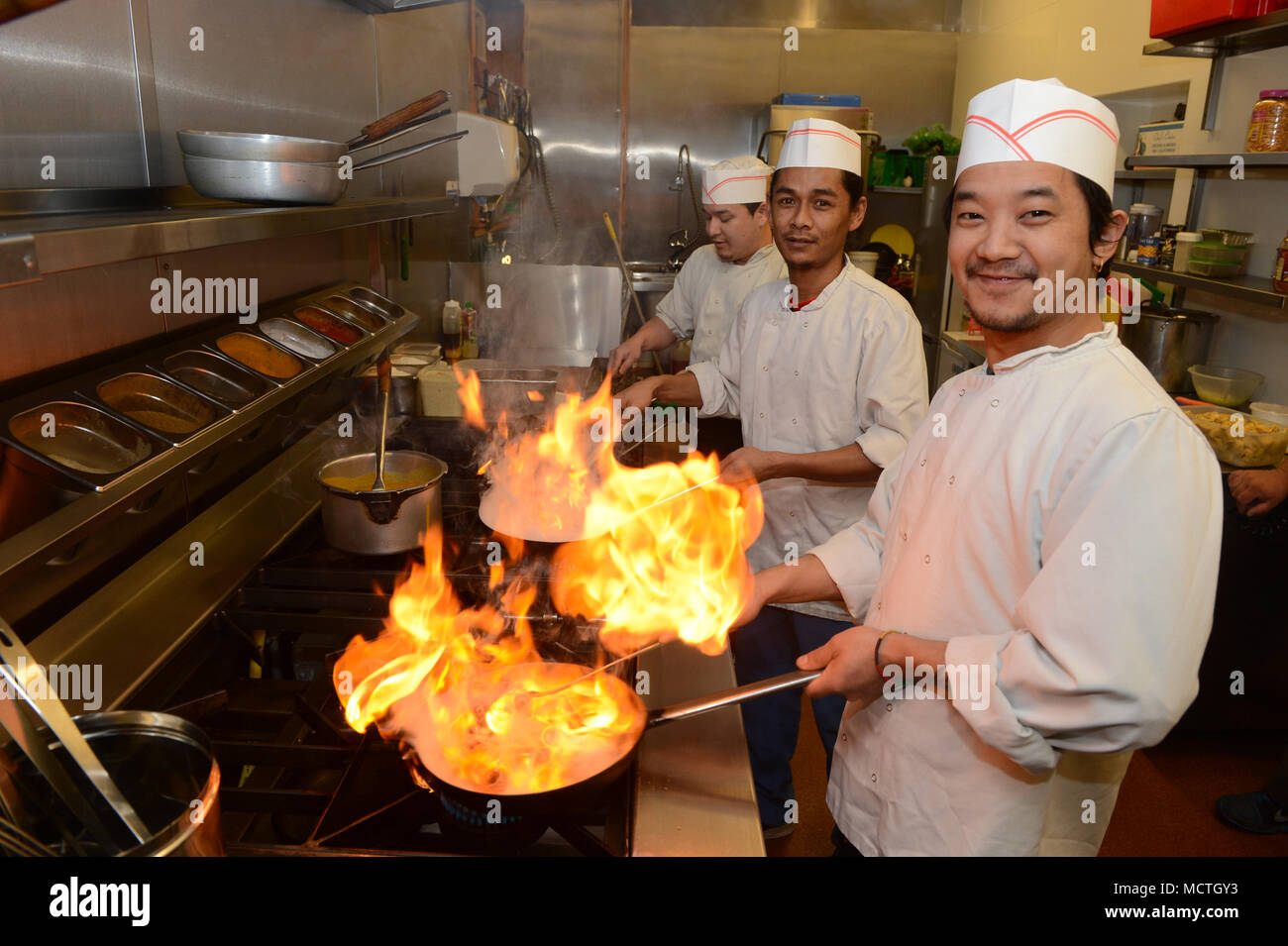 Three chefs cooking on a cooker in a restaurant making flames while ...