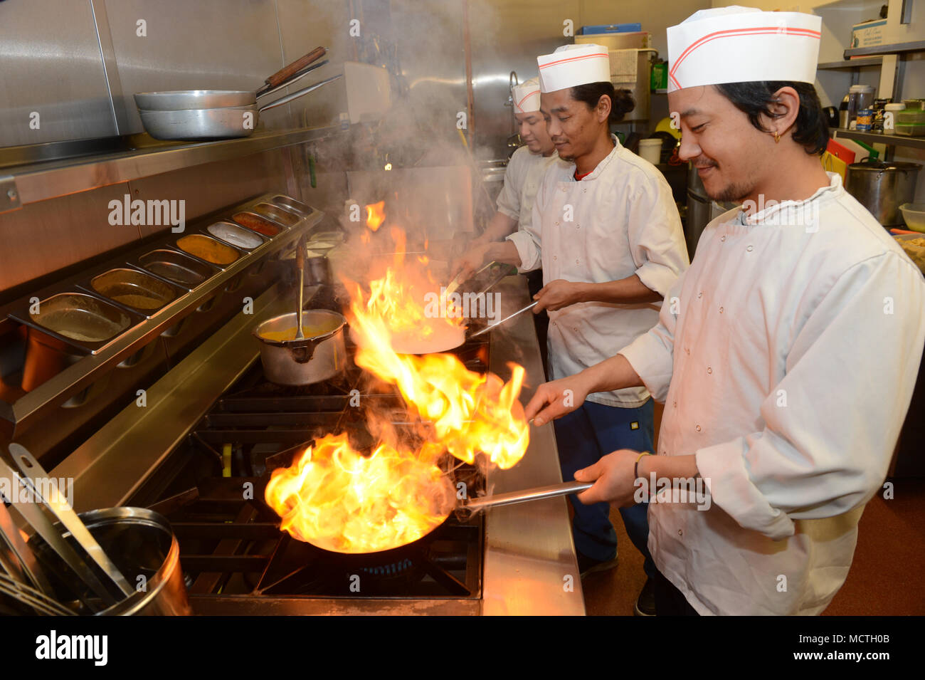 Three chefs cooking on a cooker in a restaurant making flames while ...