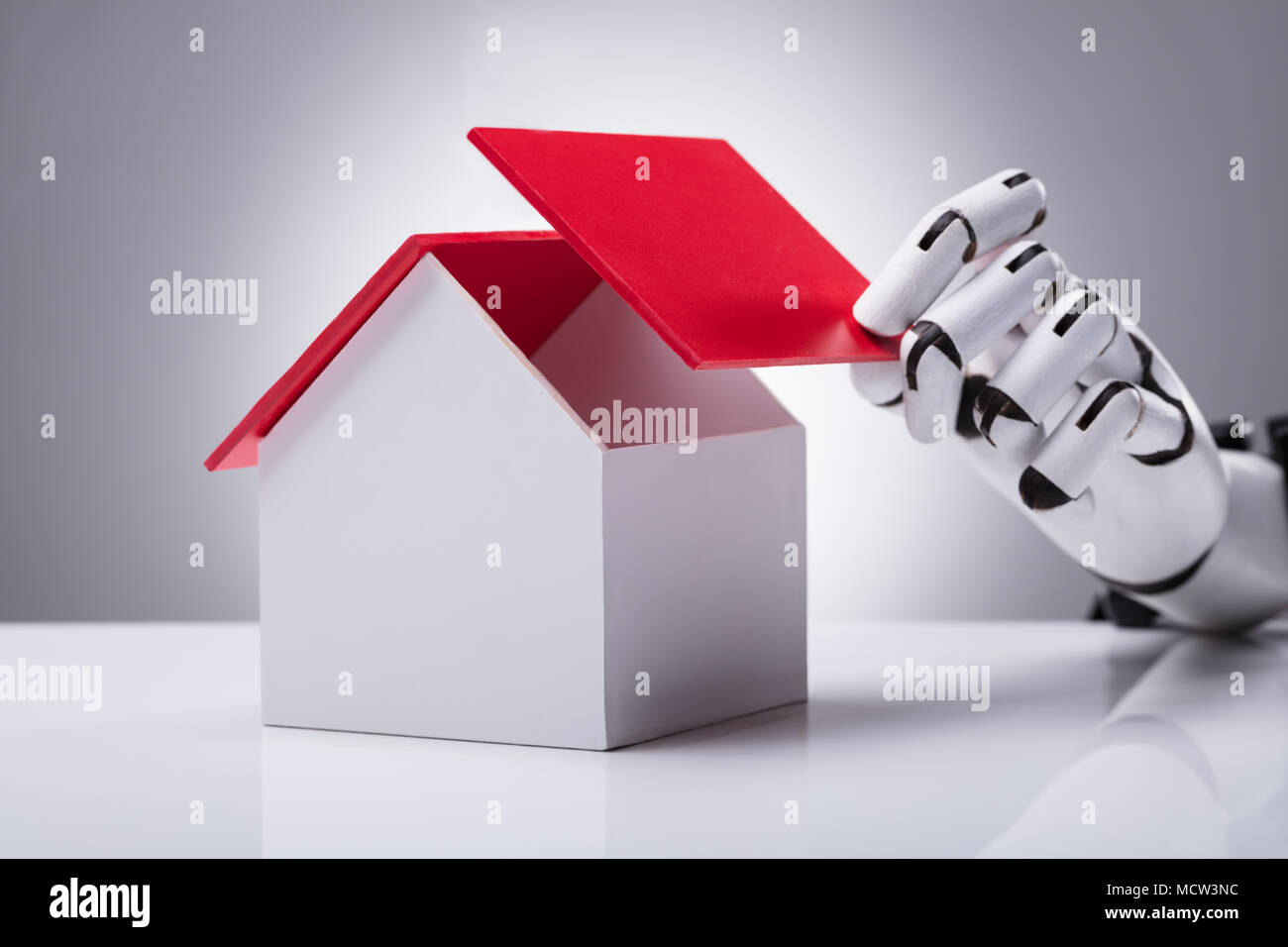 Close-up Of A Robotic Hand Building House With Red Roof Against Grey ...