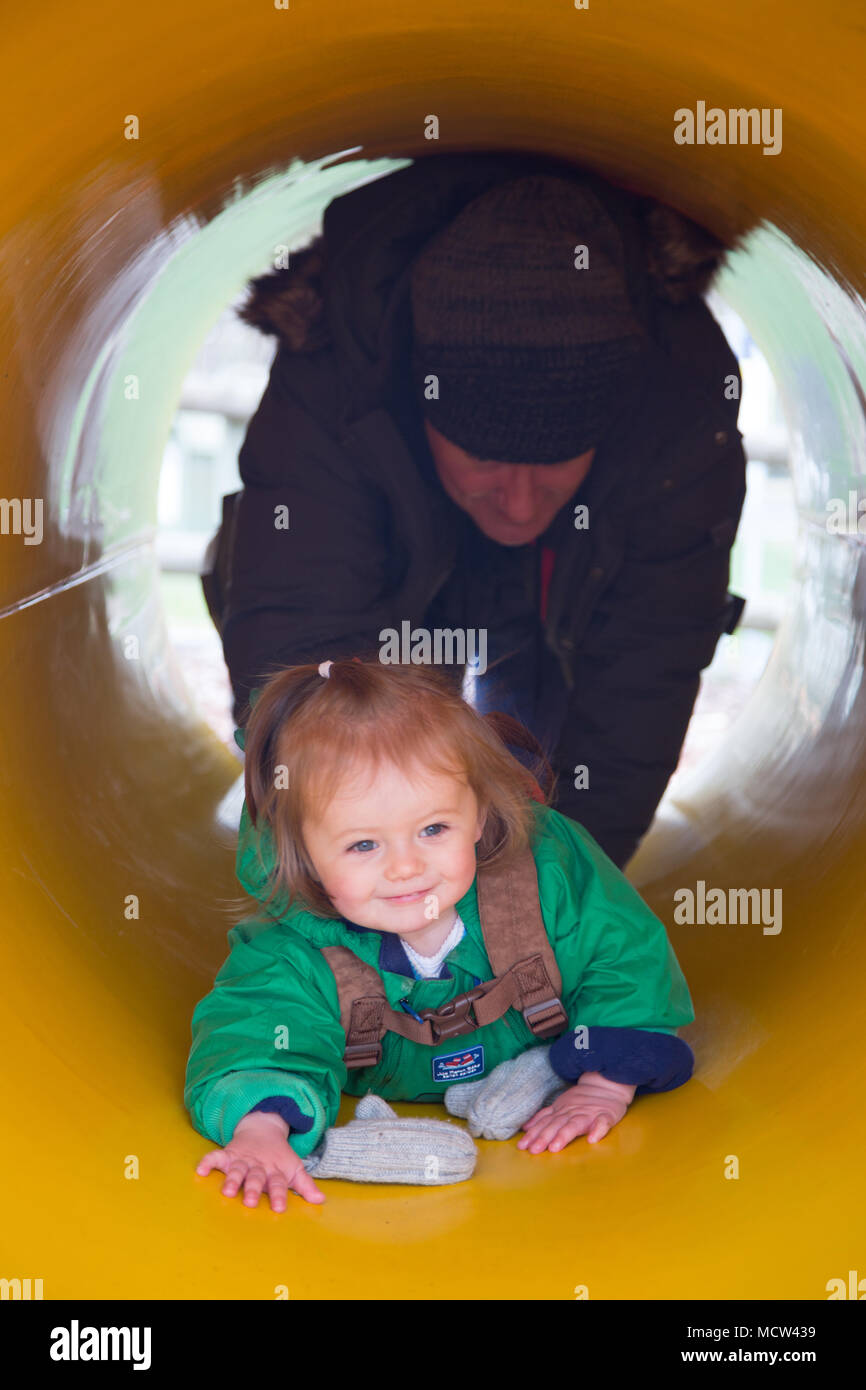 Toddler and her father crawling through a tunnel in a play park, UK ...
