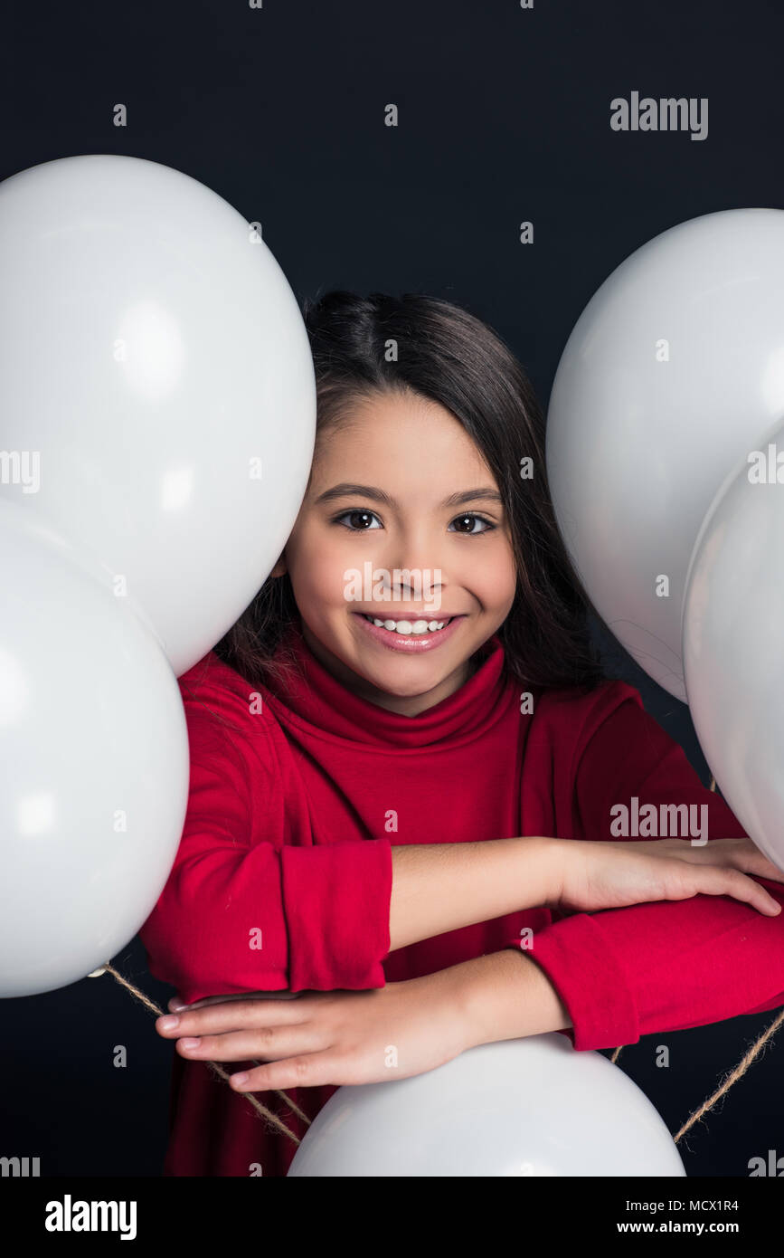Kid posing between helium balloons and looking at camera isolated on ...