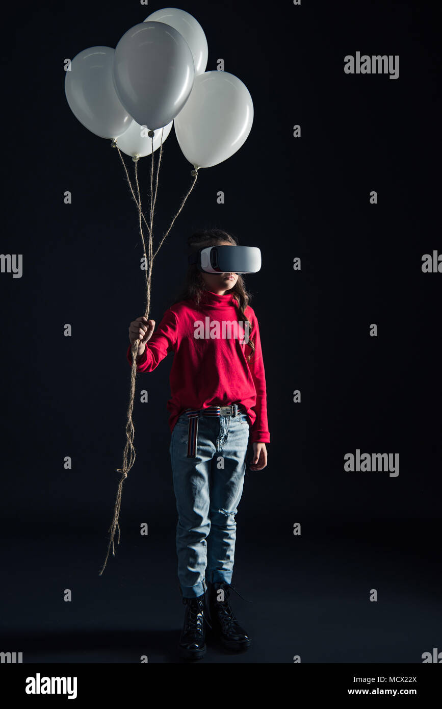 Kid in VR headset holding bundle of balloons isolated on black Stock ...