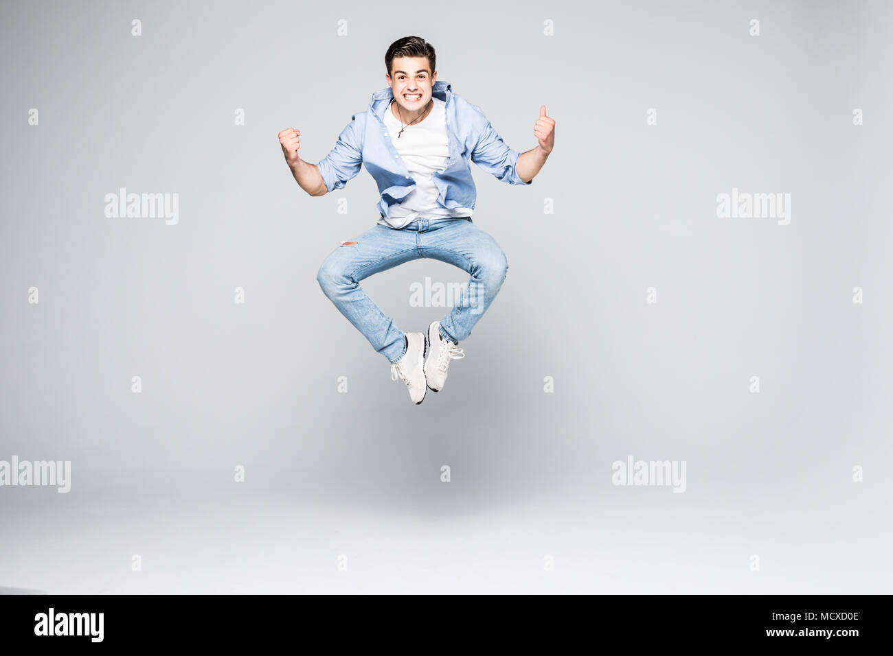 Vertical image of happy man in shirt and jeans which jumping in studio ...