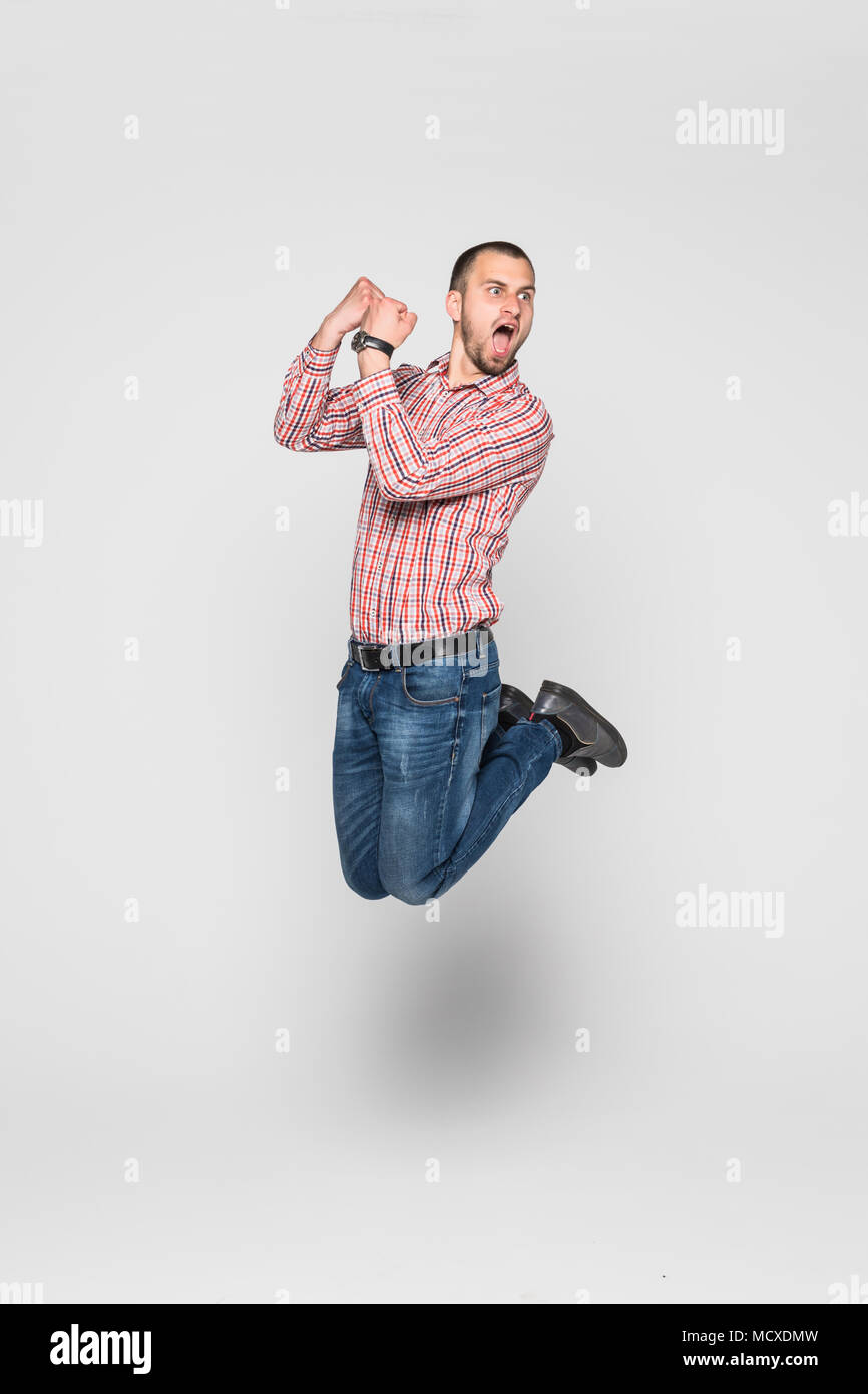 Vertical image of happy man in shirt and jeans which jumping in studio ...
